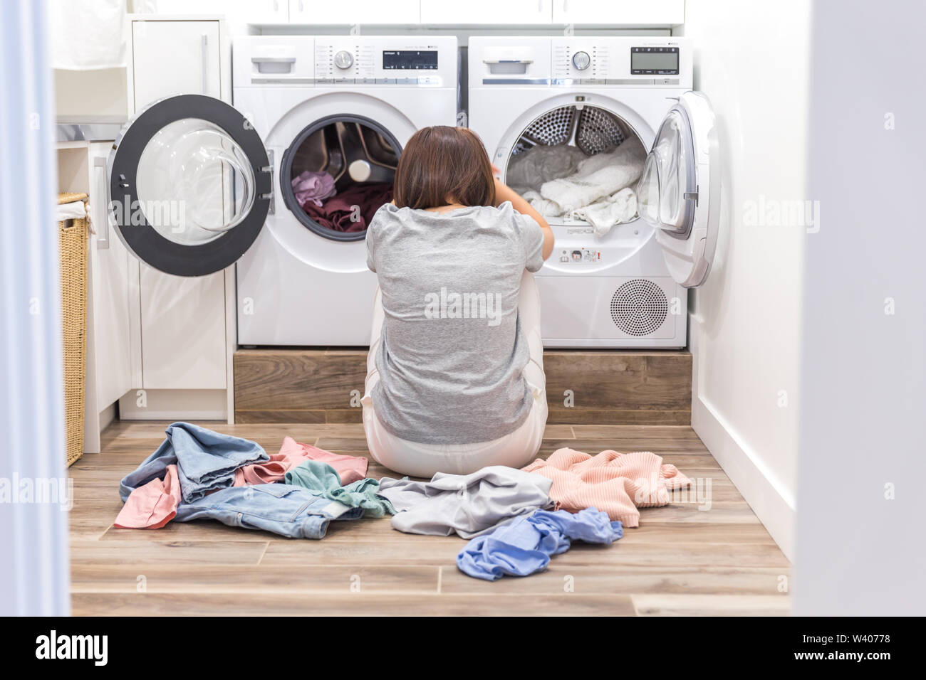 Young Tired sad Woman sitting on the floor in laundry room, back view ...