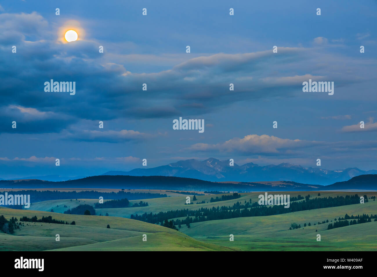full moon setting above peaks of the flint creek range and foothills ...