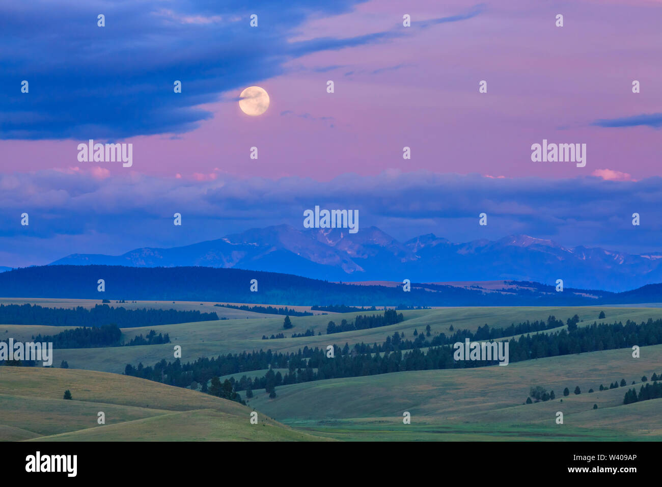 full moon setting above peaks of the flint creek range and foothills ...