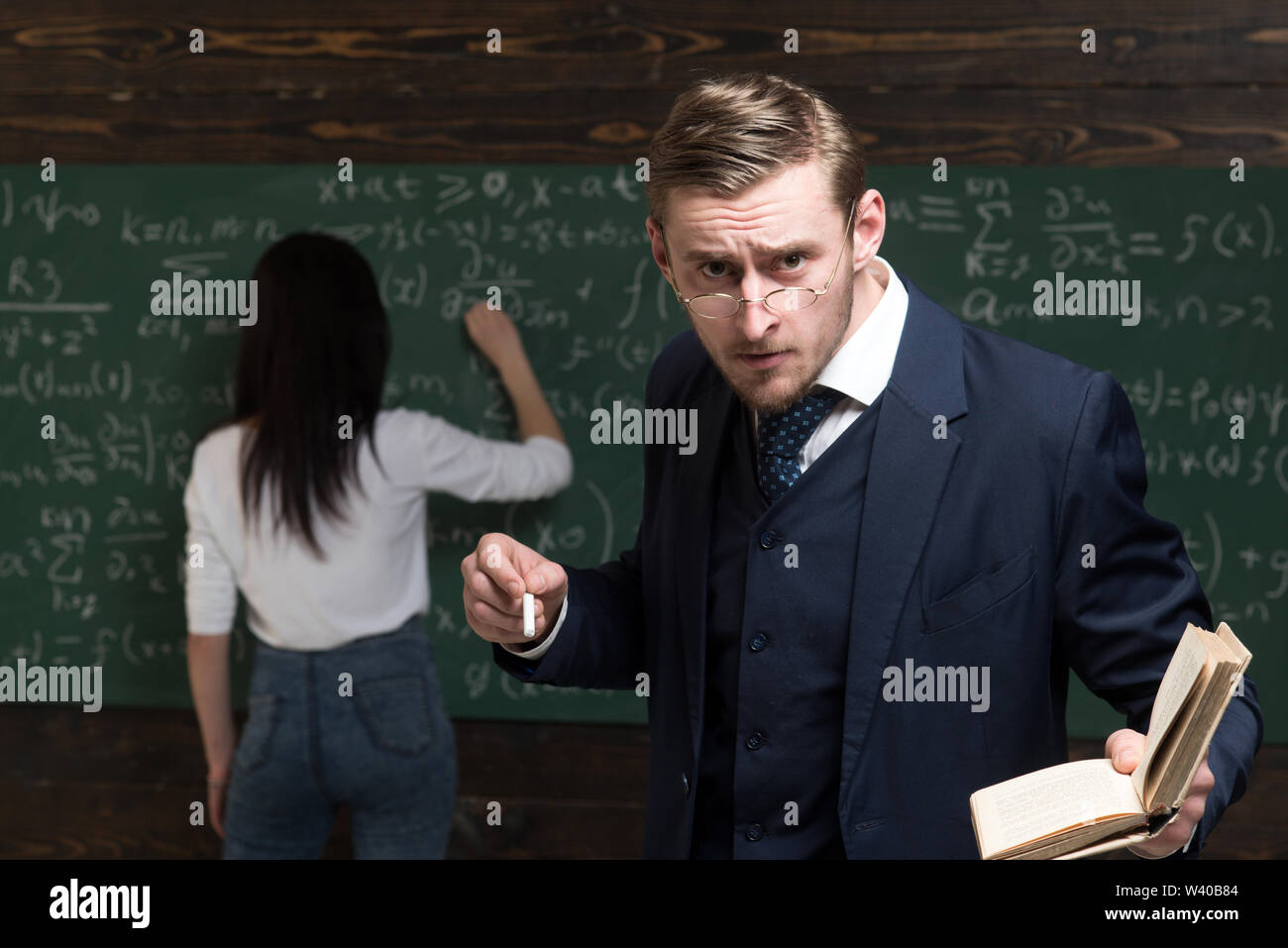 Strict professor looking at students over the glasses while holding ...