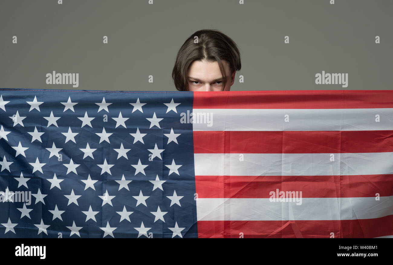 Man on serious face holds flag of USA, hiding behind flag. Guy hiding ...