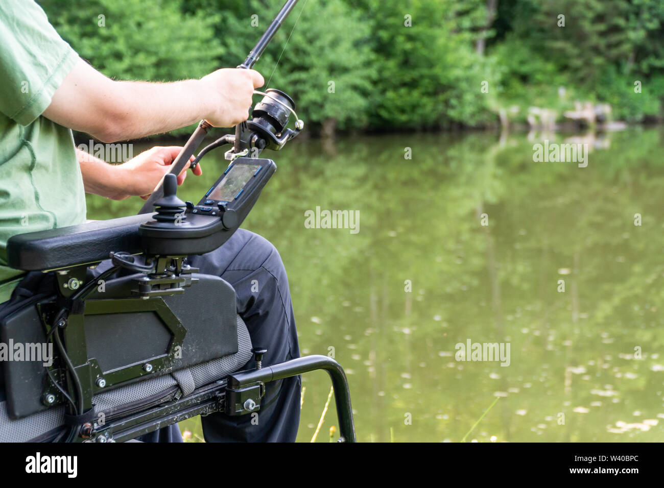 closeup of a man in a electric wheelchair fishing at the beautiful pond ...