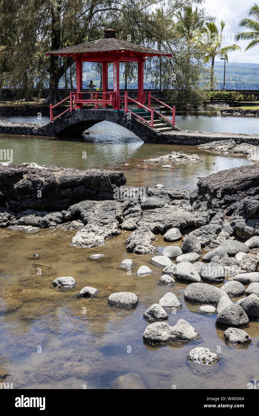 A red covered bridge at the park in Hilo, Hawaii with rocky shoreline ...