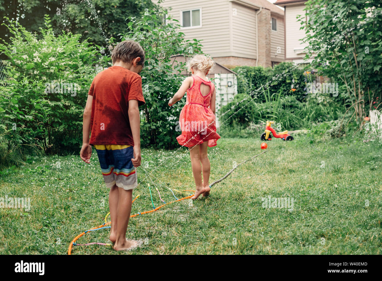 Kids friends splashing with gardening hose sprinkler on backyard on ...
