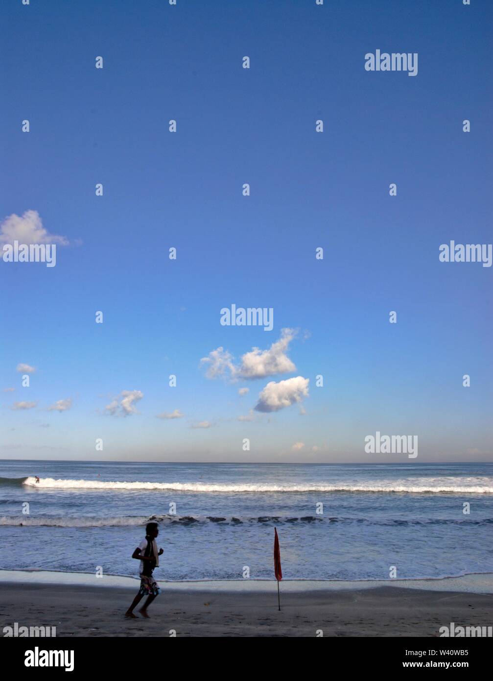 Kuta Beach, Bali, Indonesia - June 2019 : A man runs on a beach with a ...