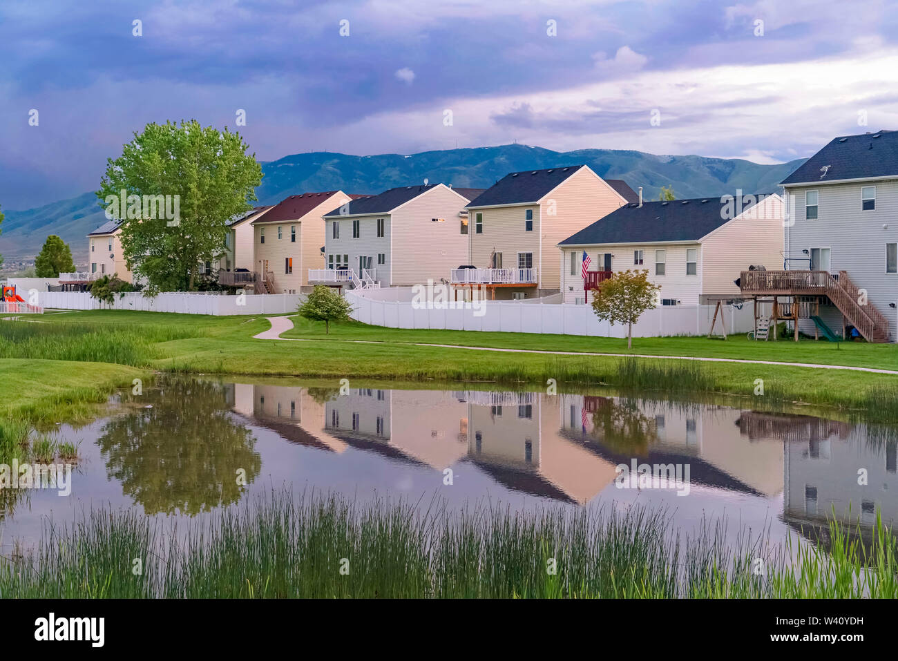 Shiny pond and pathway amid a grassy terrain in front of homes with ...