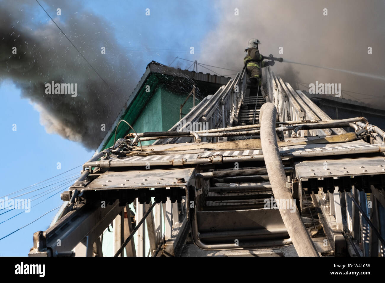 Firefighters on the stairs extinguish a fire on the roof of a ...