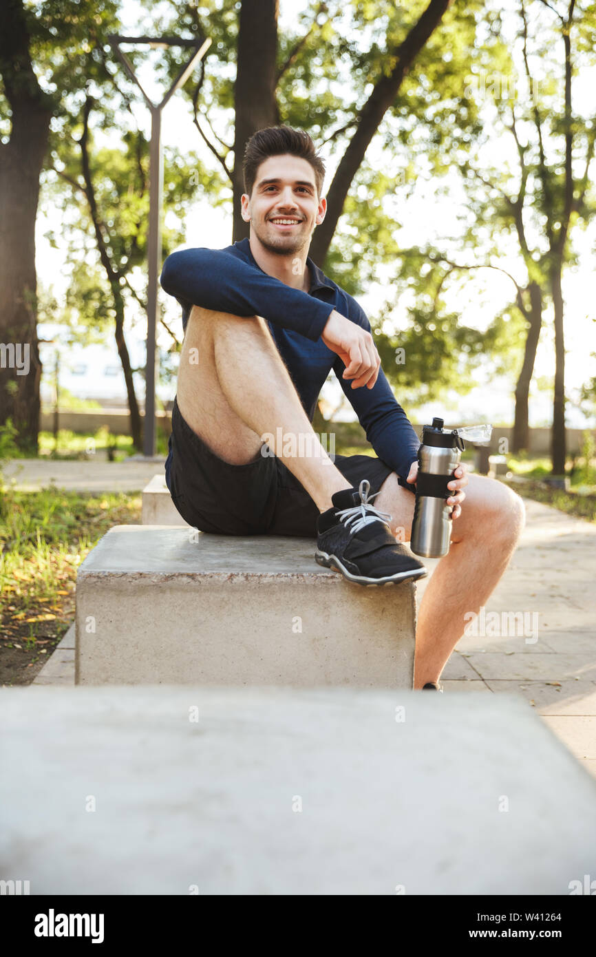 Portrait of young athletic man dressed in sportswear sitting on bench ...
