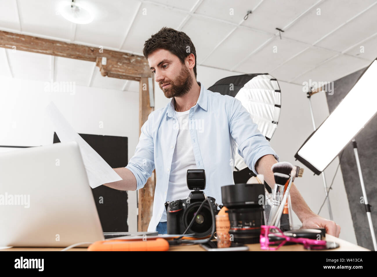 Portrait of masculine brunette photographer man using laptop while ...