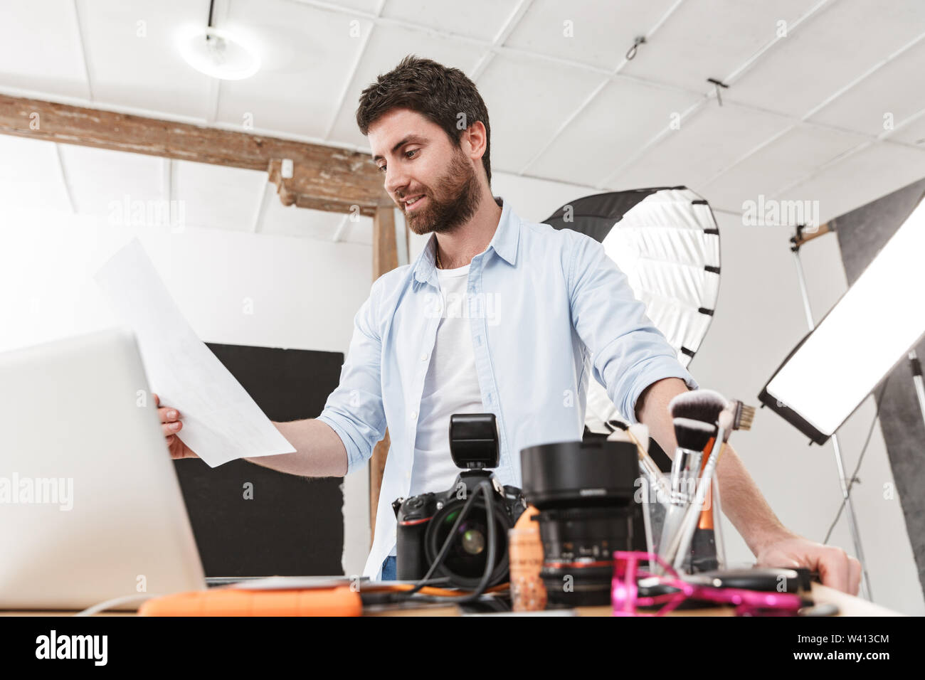 Portrait of creative brunette photographer man using laptop while ...