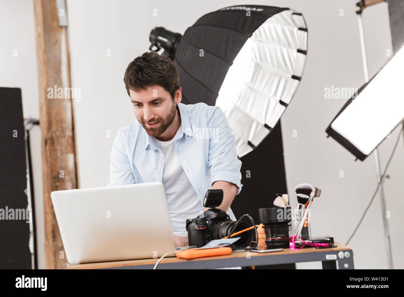 Portrait of working brunette photographer man using laptop while ...