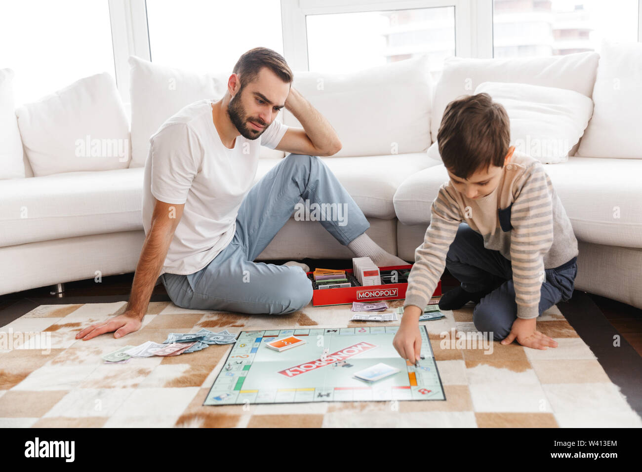 Cheerful young father playing monopoly with his little son while ...