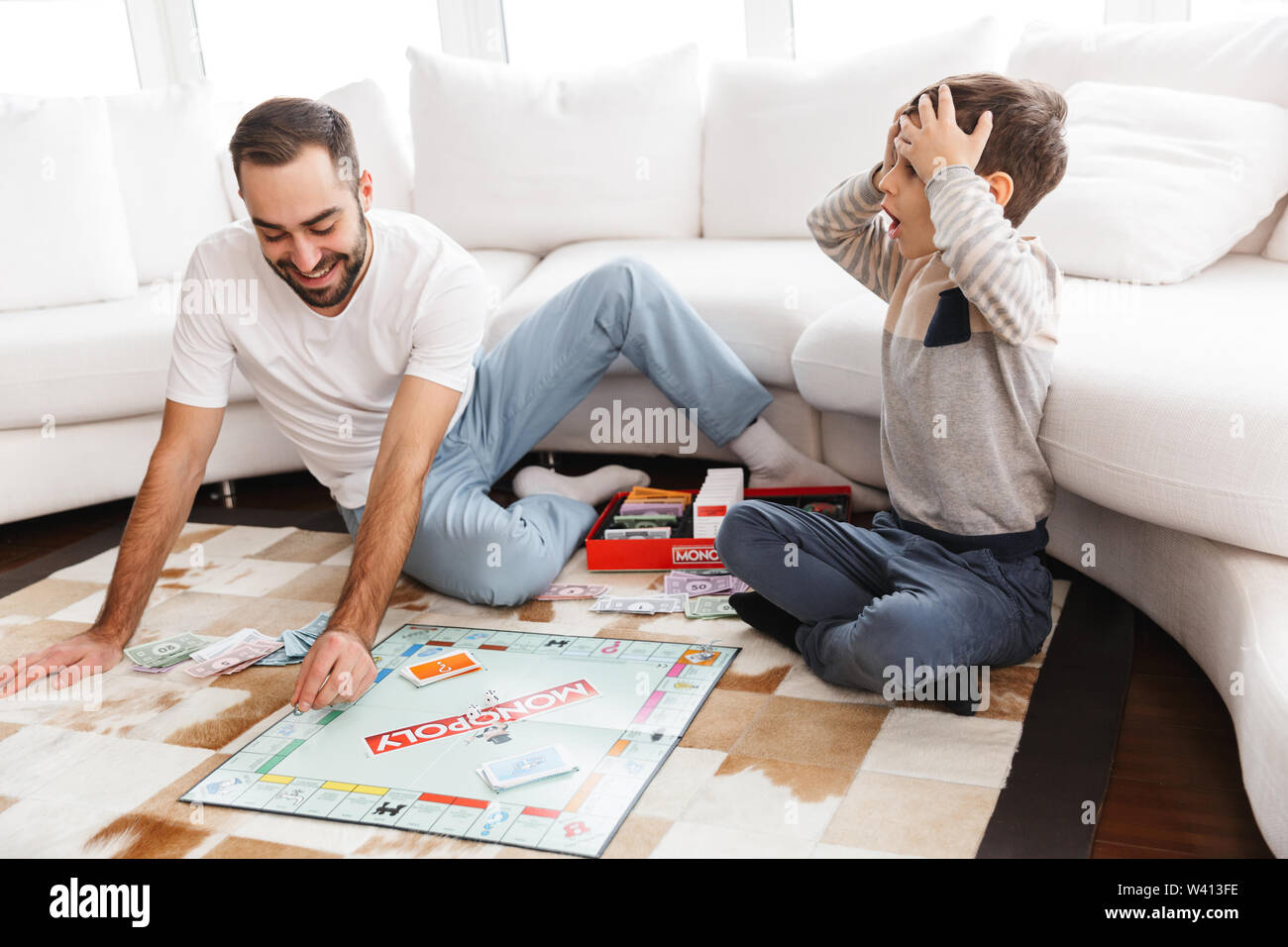 Cheerful young father playing monopoly with his little son while ...