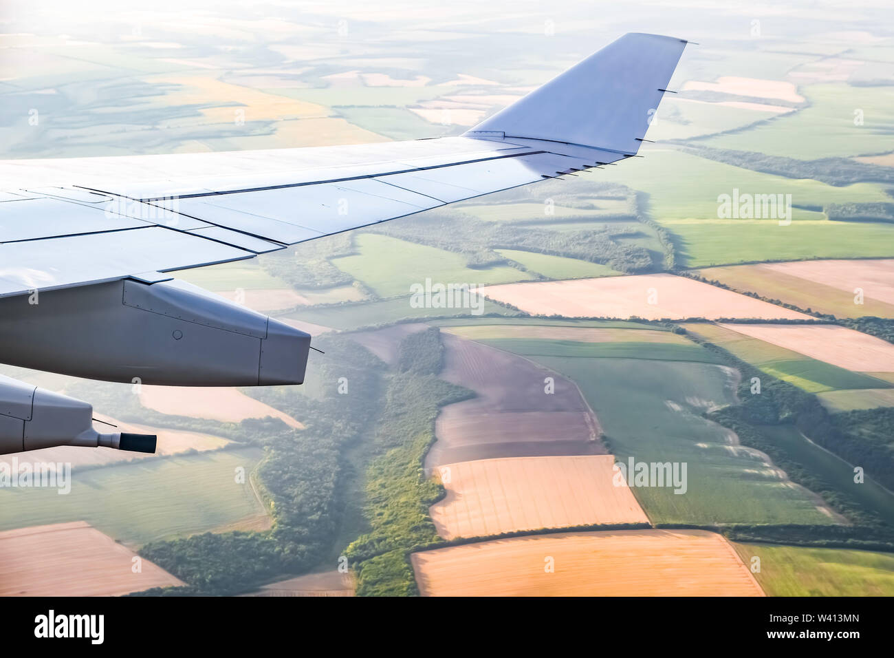 Large wing of passenger jet plane flying over patchwork of agricultural ...
