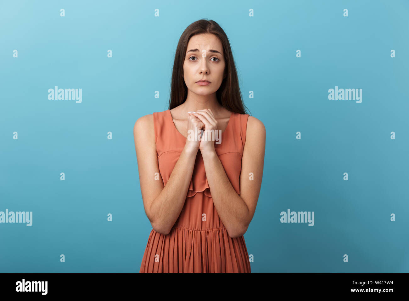 Cute lovely young girl standing isolated over blue background, praying ...