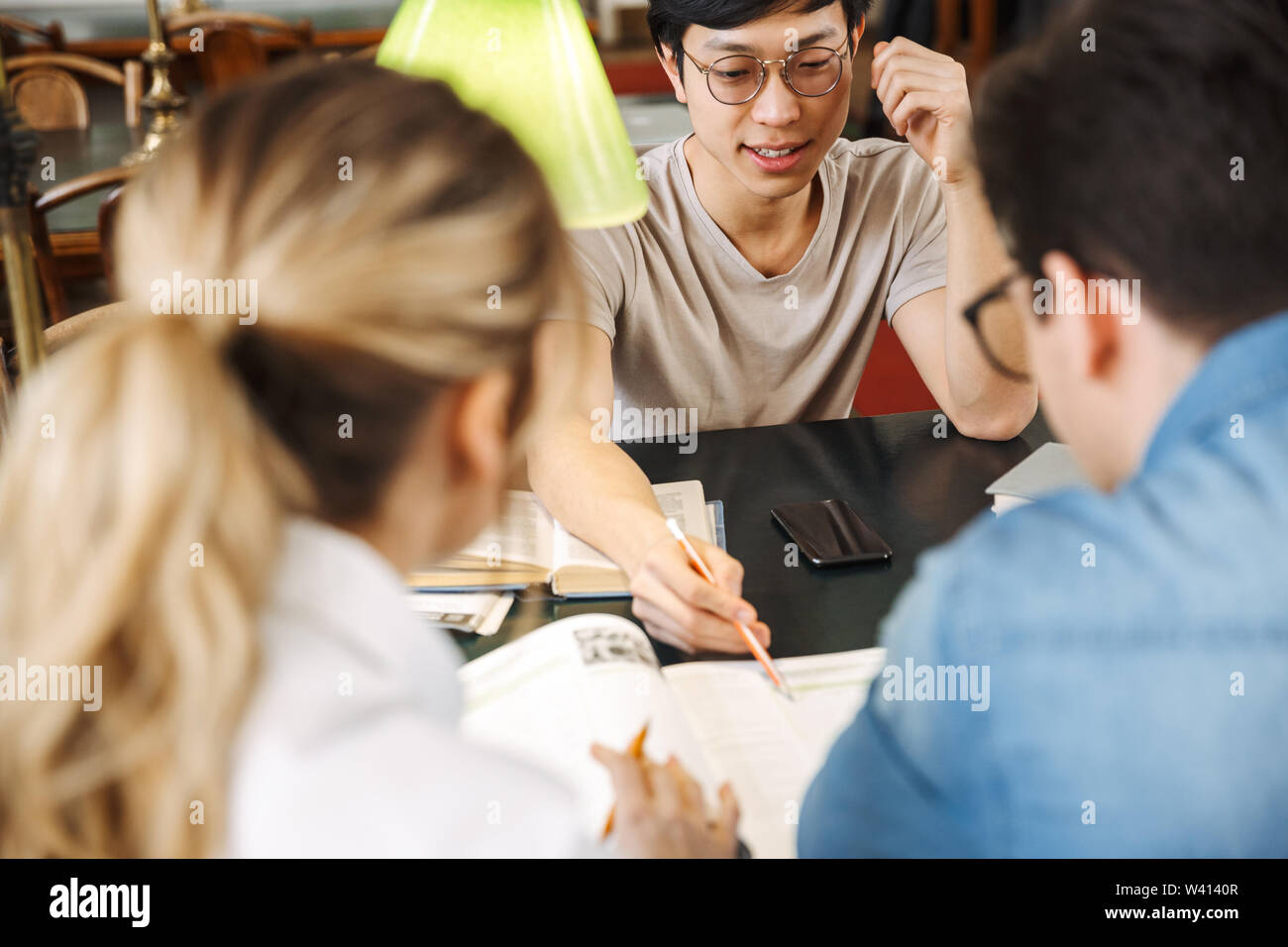 Back view of a smart teenagers studying at the library together ...