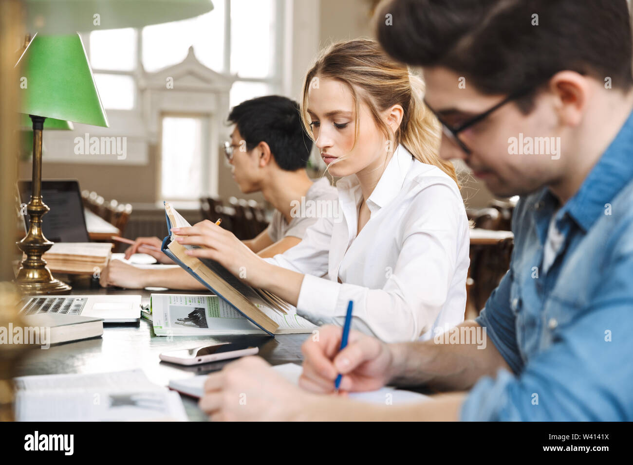 Group of smart young students studying hard at the library, using ...