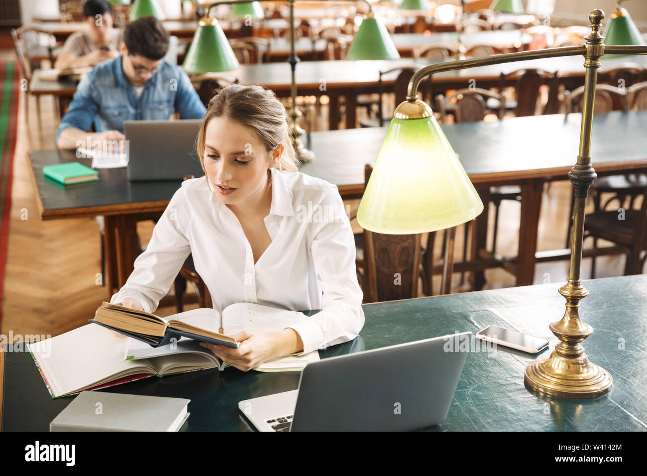 Smart cheerful teenagers studying at the library together, reading ...