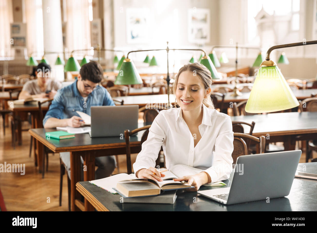 Smart cheerful teenagers studying at the library together, reading ...