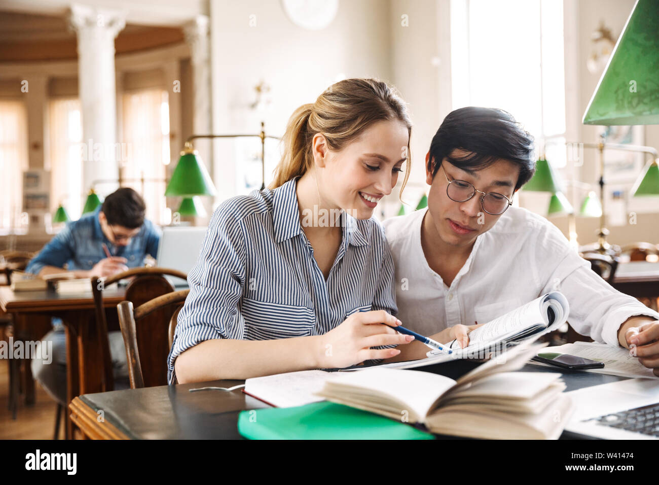Smart cheerful teenagers studying at the library together, reading ...