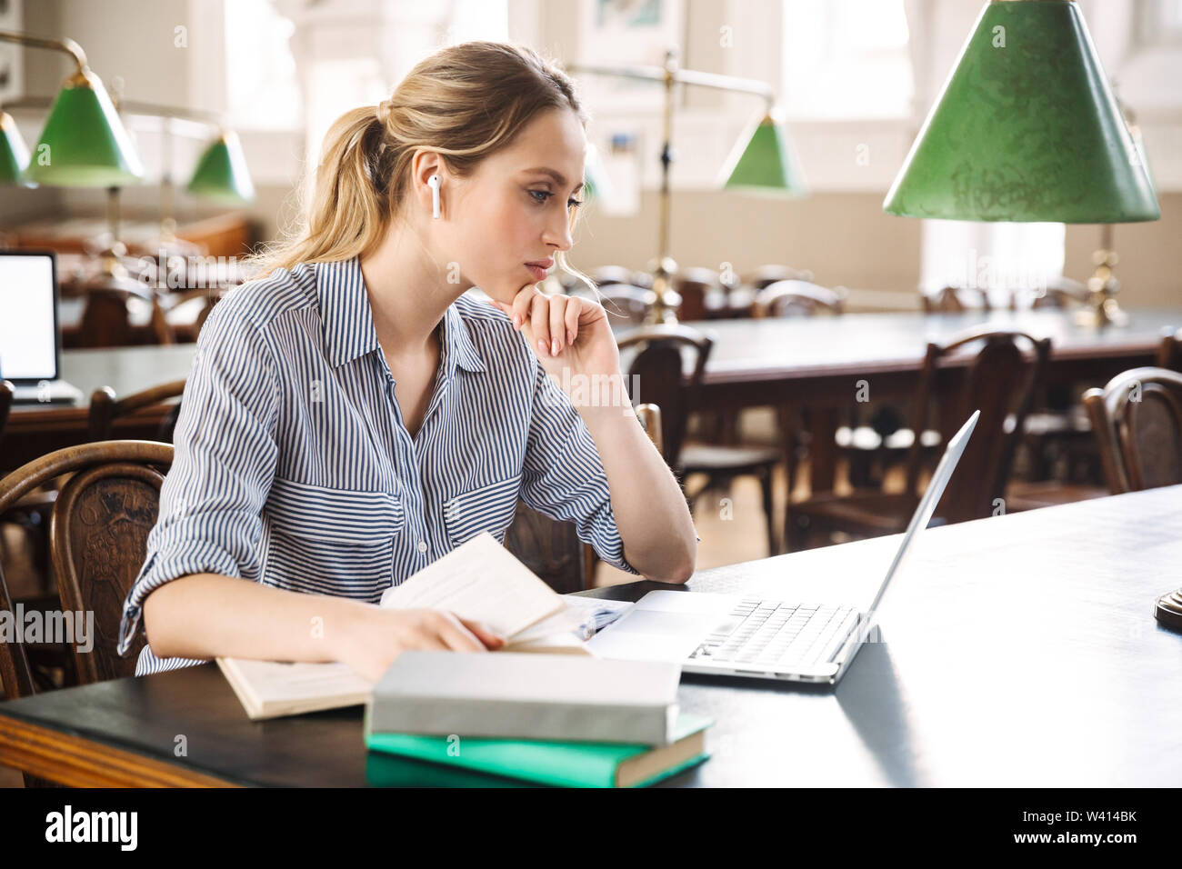 Attractive blonde girl student studying at the library with laptop ...