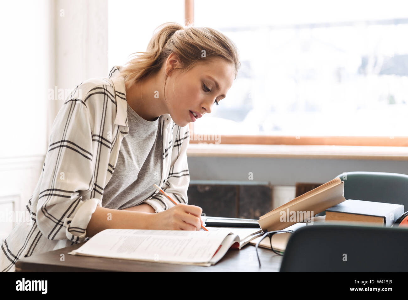 Attractive young girl student doing homework at the cafe indoors ...