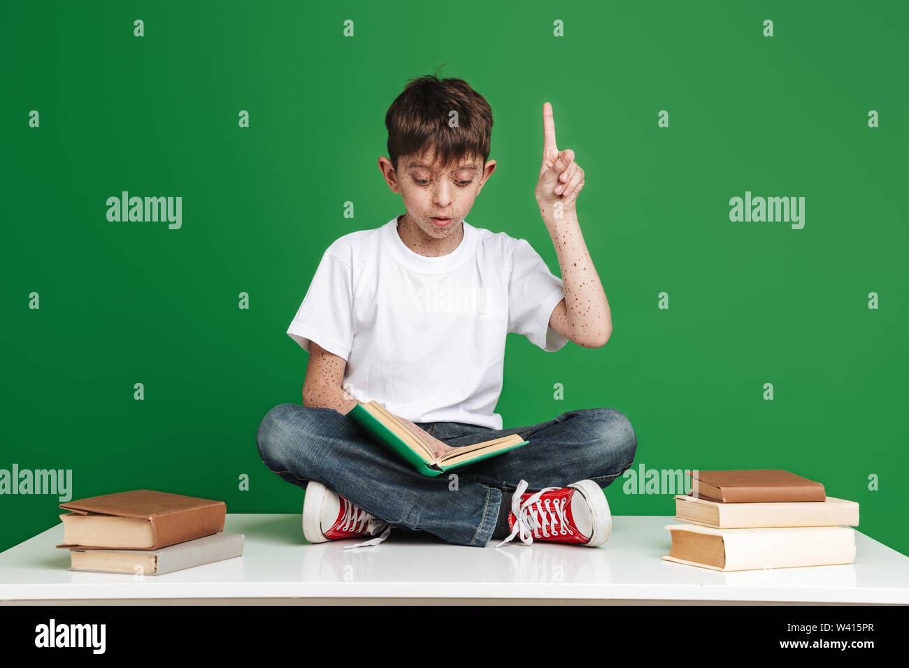 Surprised young boy with freckles reading book and having idea over ...