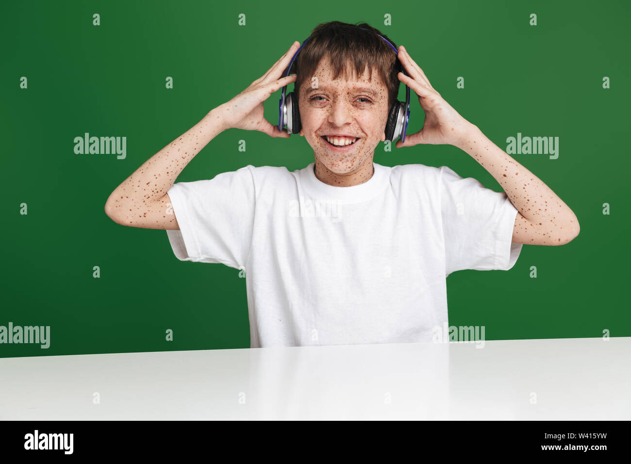 Smiling young boy with freckles in headphones listening music and ...