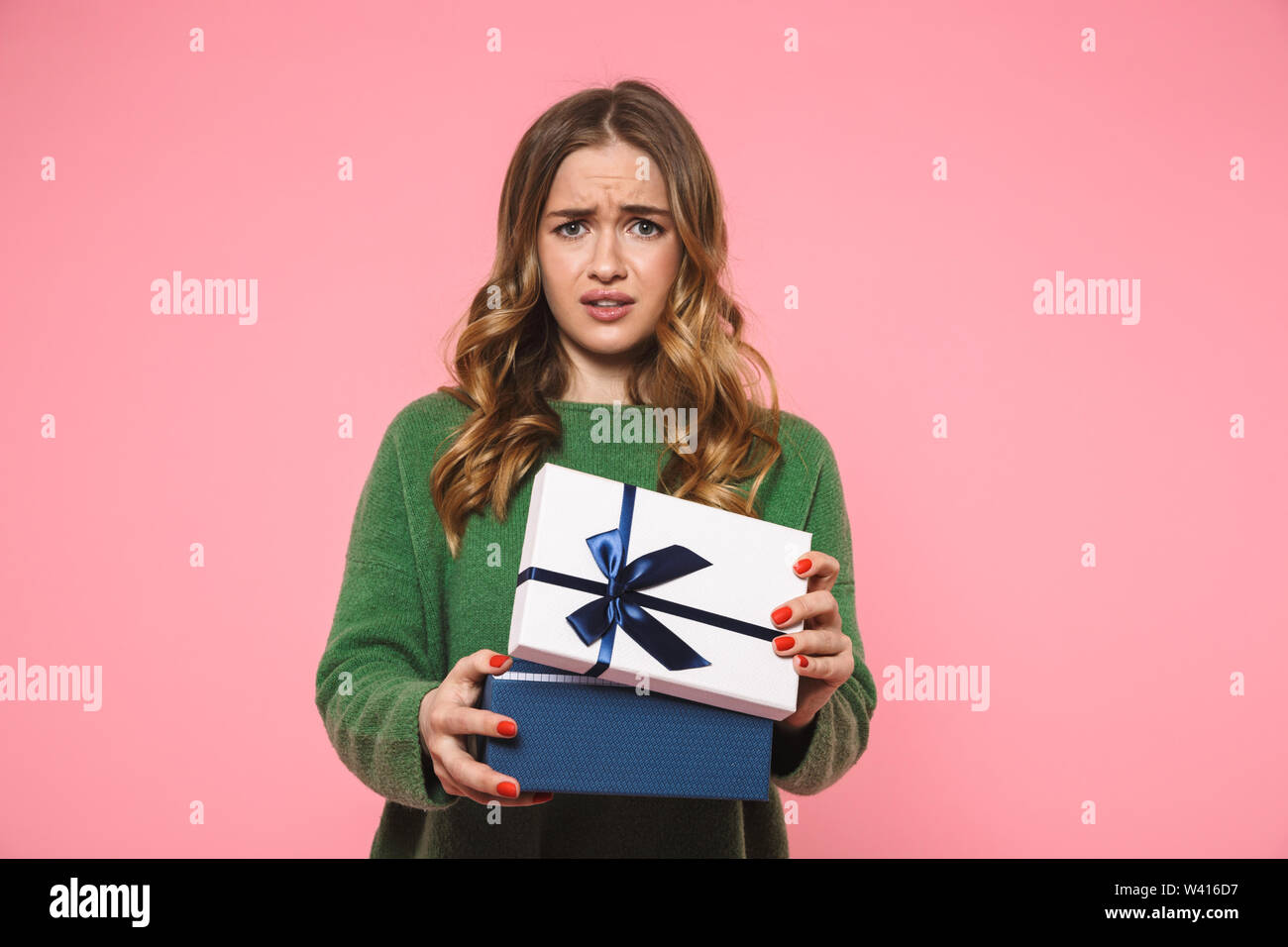 Displeased blonde woman wearing in green sweater opening gift box and ...