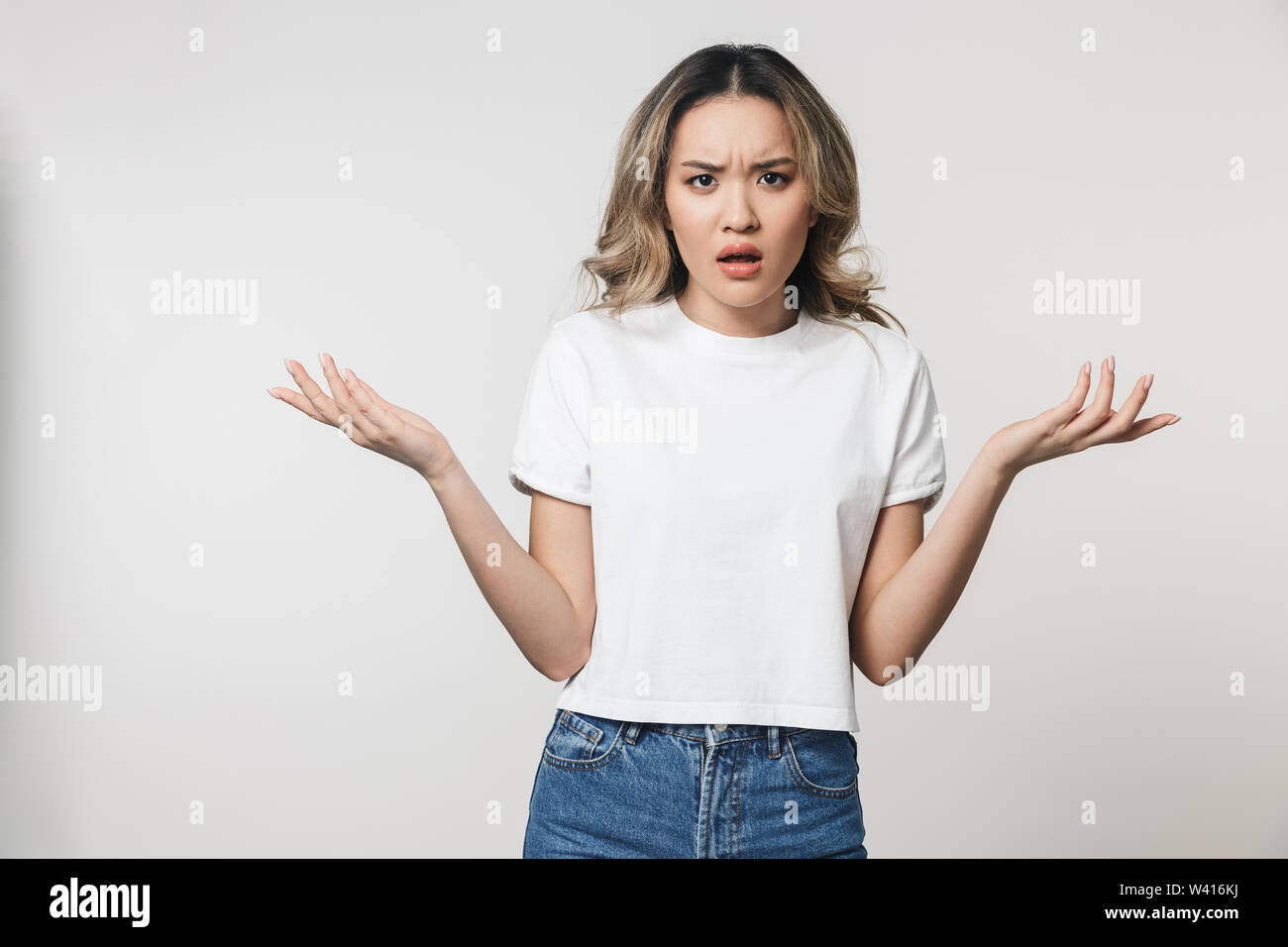 Portrait of a lovely confused young asian woman standing isolated over ...