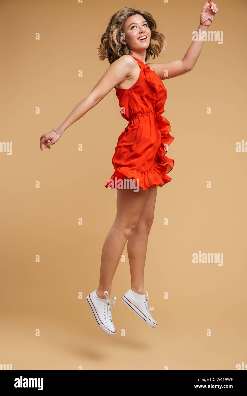 Full length of a lovely young girl wearing dress jumping isolated over ...