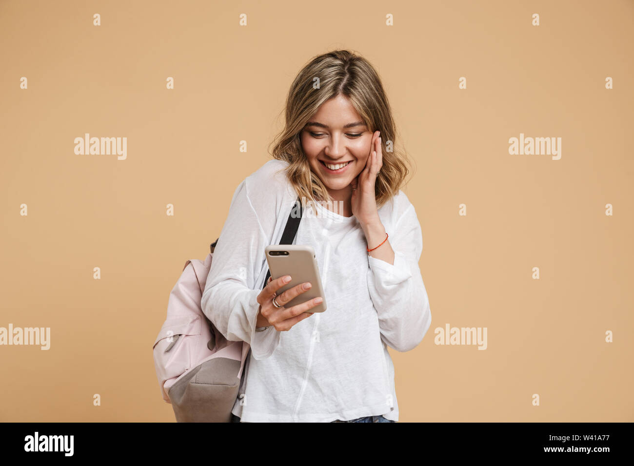 Image of nice teenage girl wearing backpack using cellphone and smiling ...