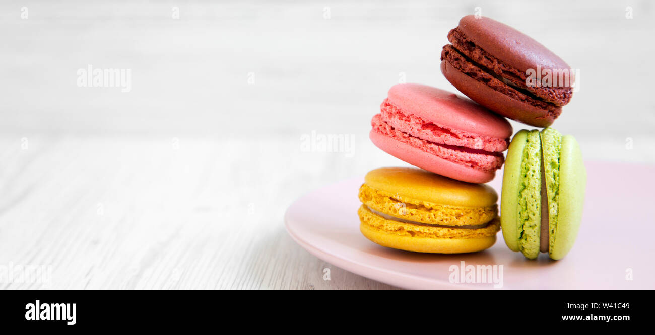 Sweet and colorful macarons on a pink plate over white wooden ...
