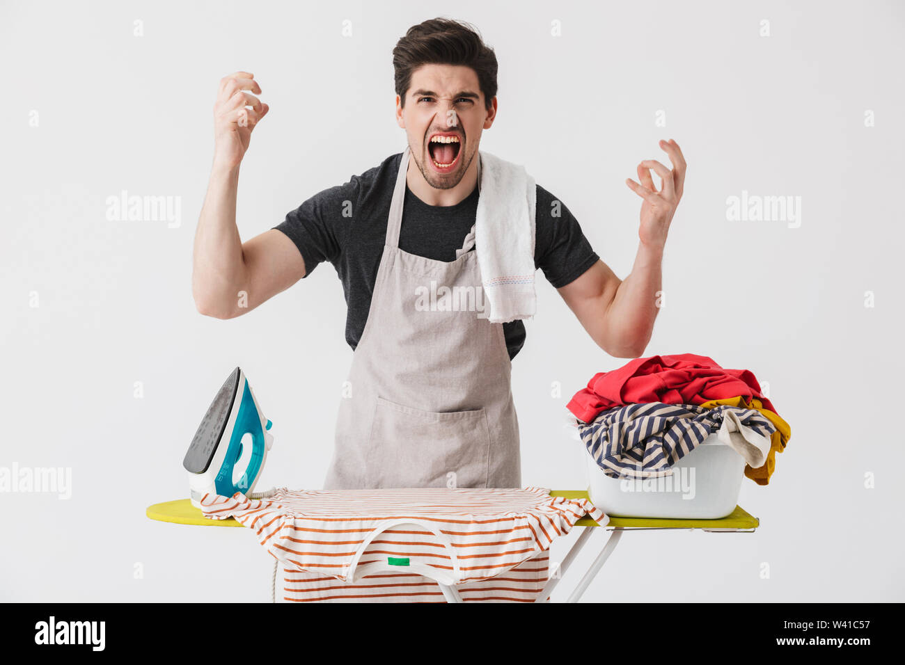 Handsome angry brunette houseman wearing apron standing isolated over ...