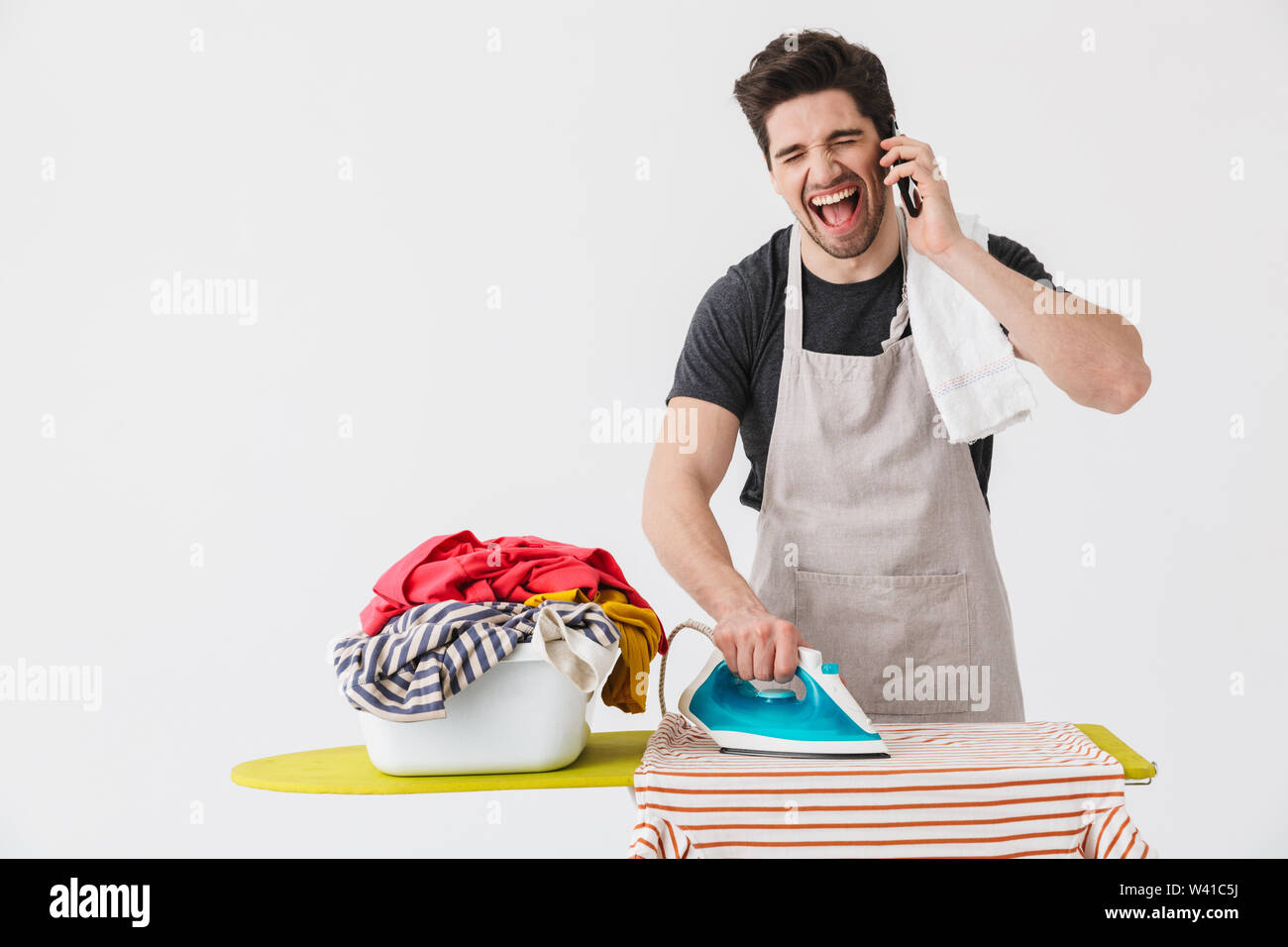 Handsome angry brunette houseman wearing apron standing isolated over ...