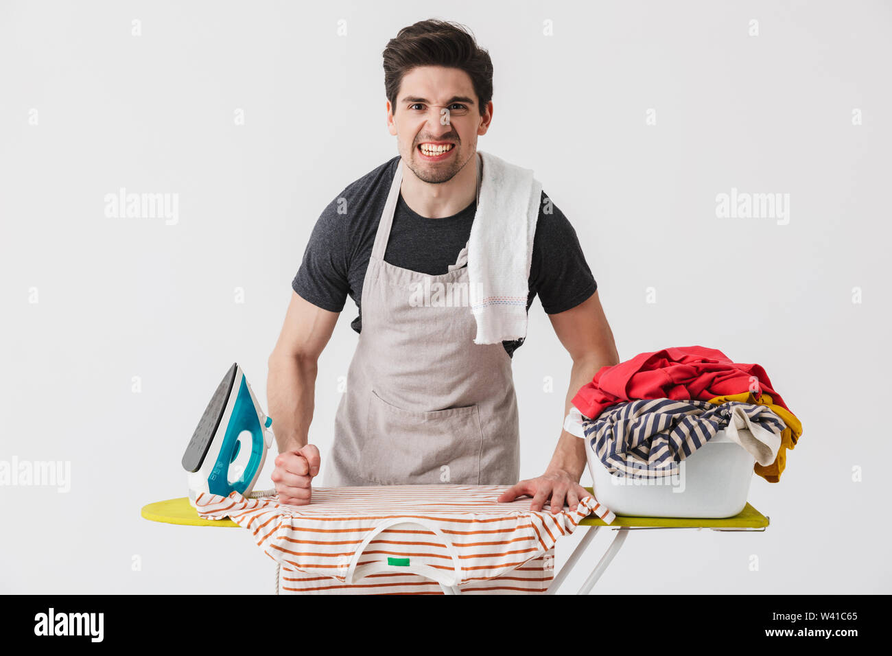 Handsome angry brunette houseman wearing apron standing isolated over ...