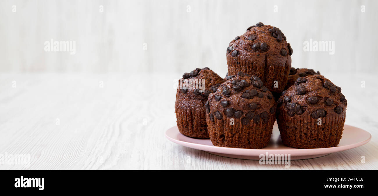 Chocolate cupcakes on a pink plate over white wooden background, side ...