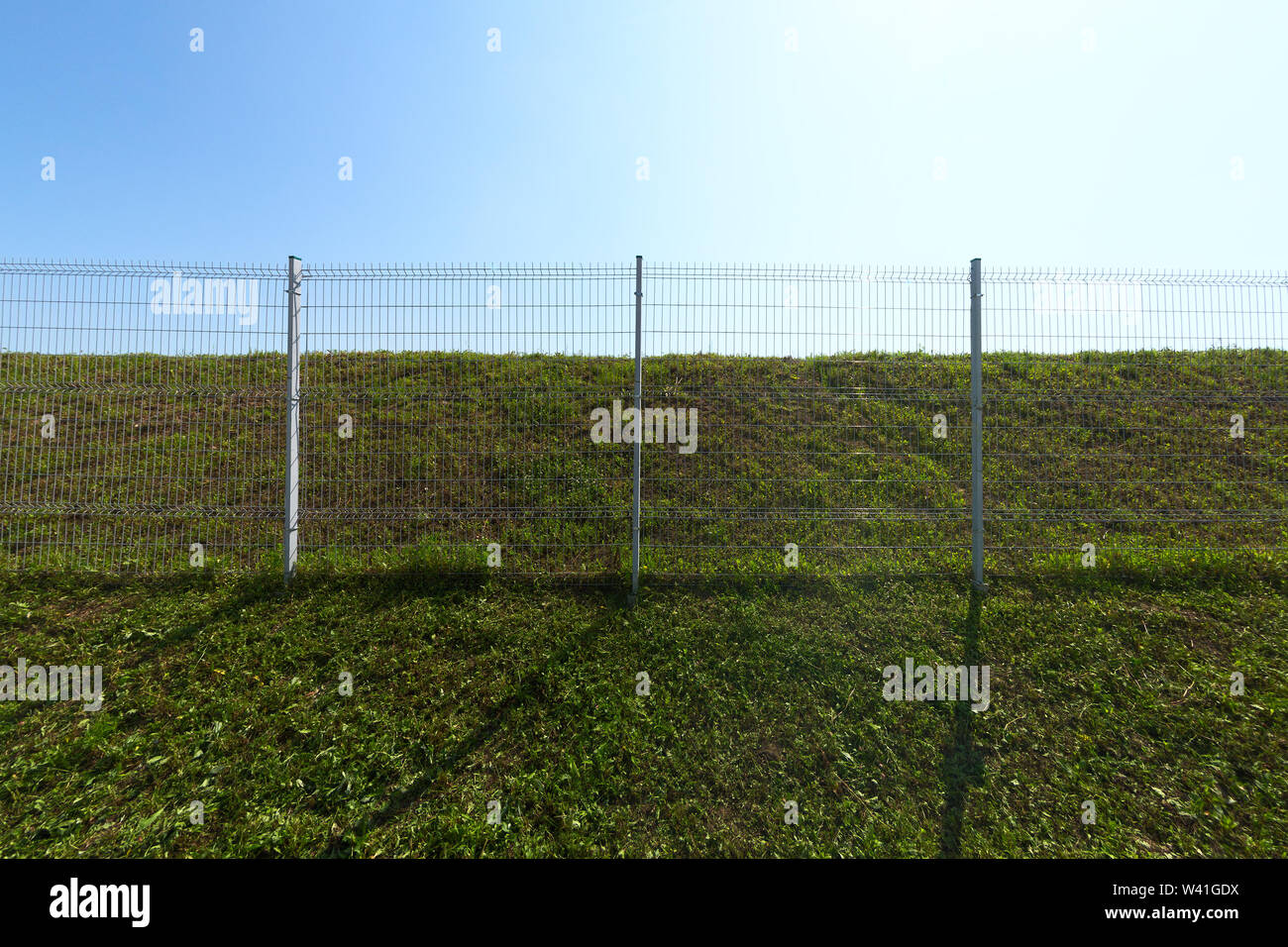 Metal wire industrial grid fence on green grass with blue sky ...