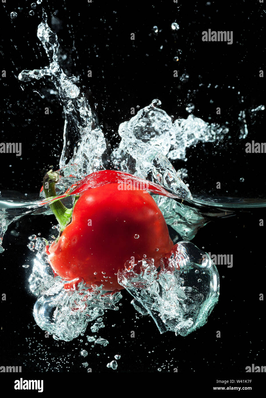 Sweet red pepper plopping in the clear water with many splashes on a ...