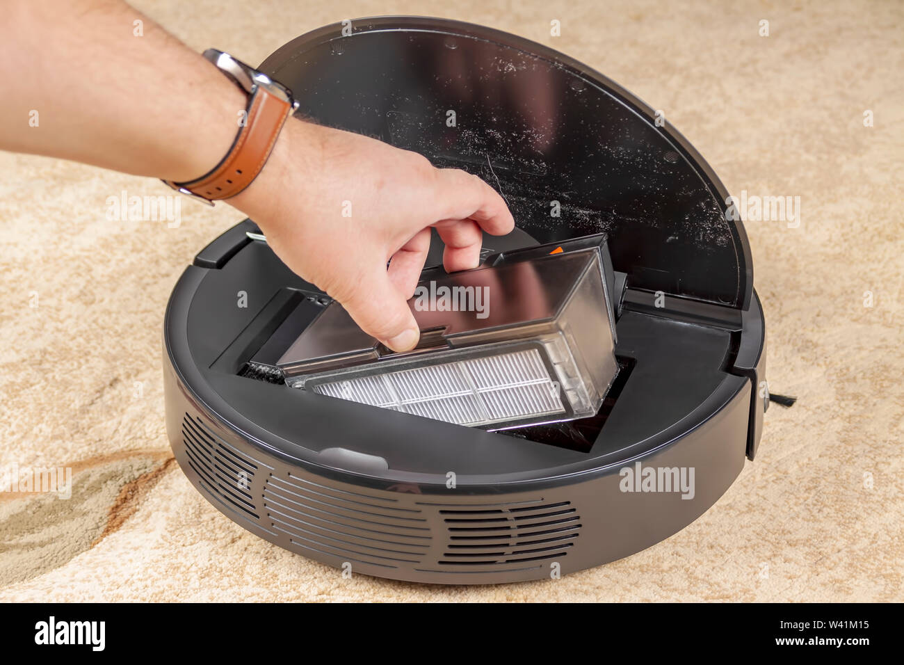 The hand pulls out a container of garbage from the robot vacuum cleaner ...