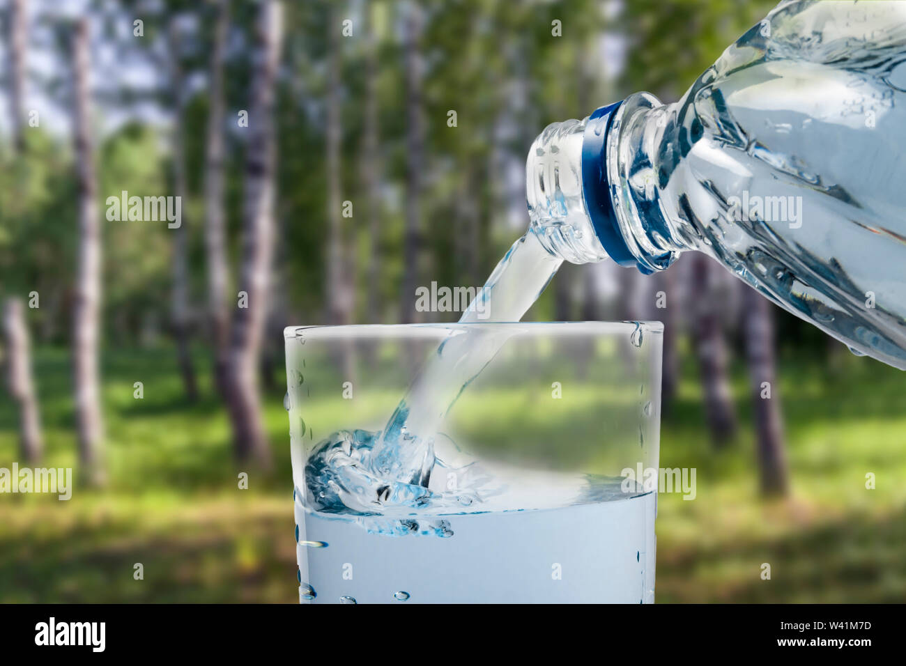 From a bottle of water flows into a glass on the background of summer ...