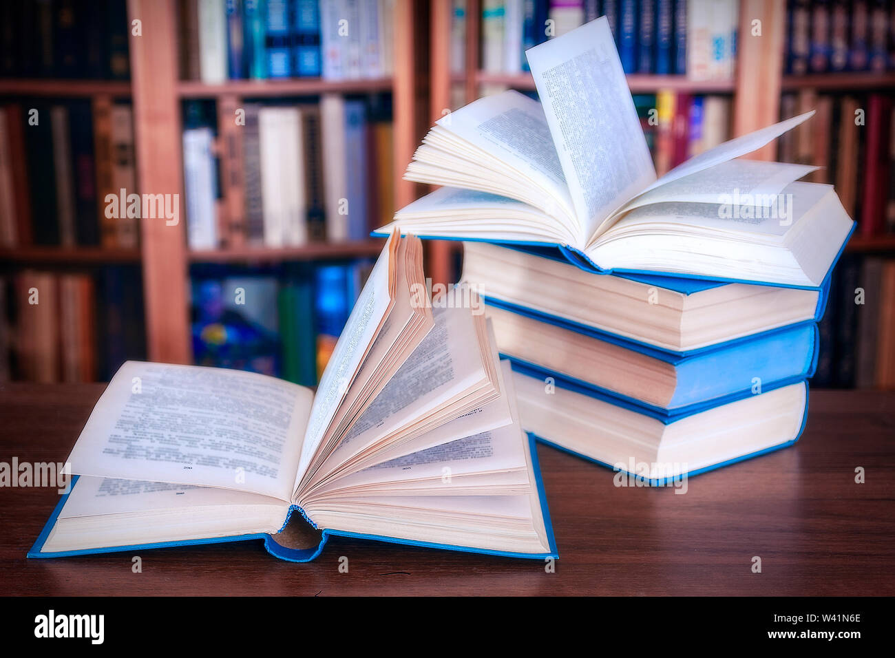 Book stack on wood desk and blurred bookshelf in the library room ...