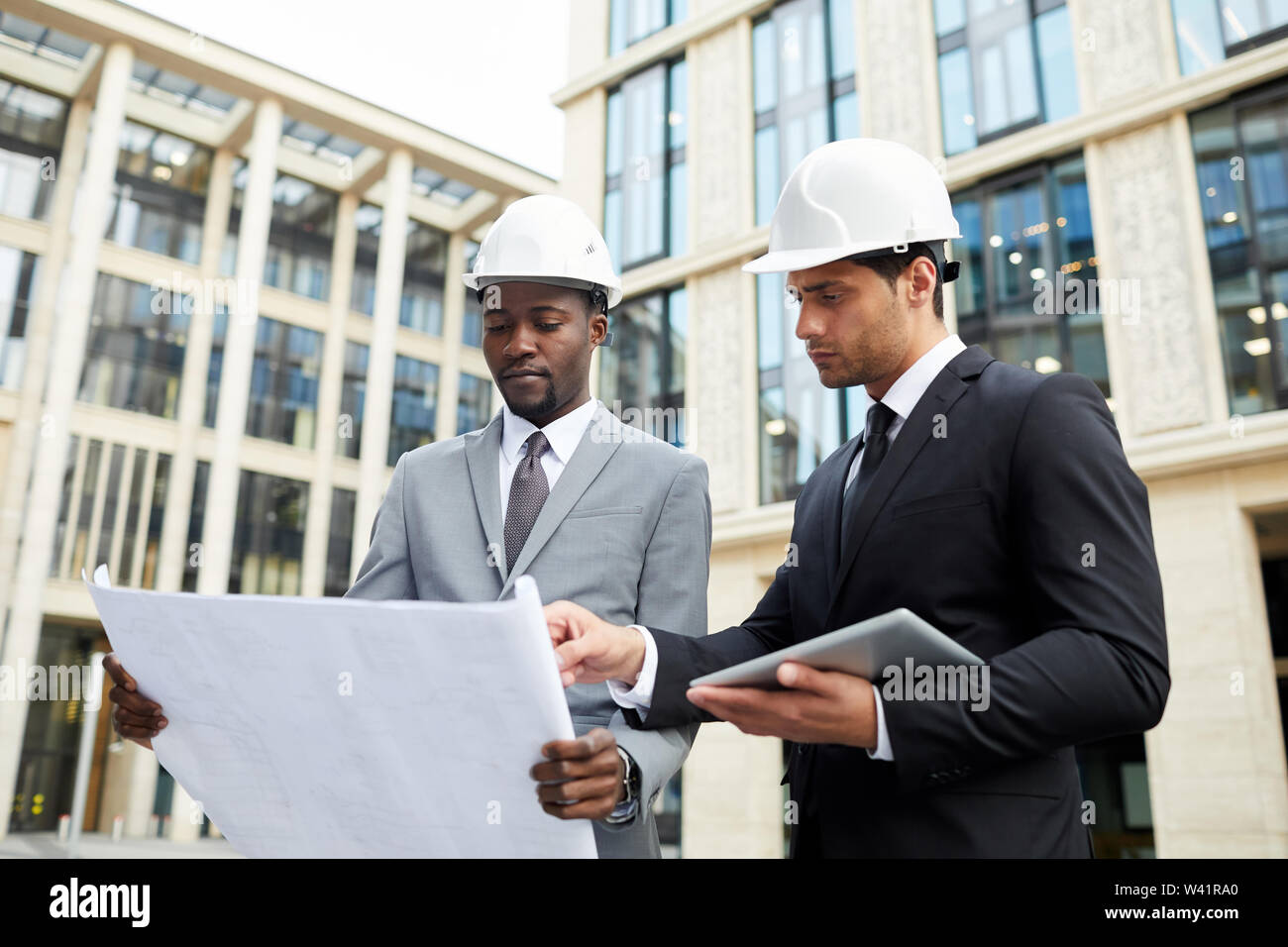 Two engineers in suits and helmets discussing project of new building ...