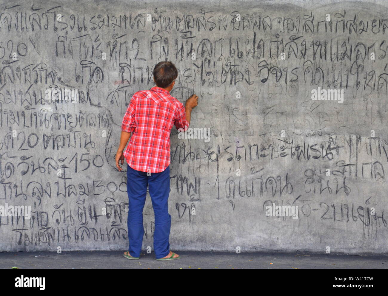 A senior Asian man writes on a wall in Thai script in Bangkok, Thailand ...