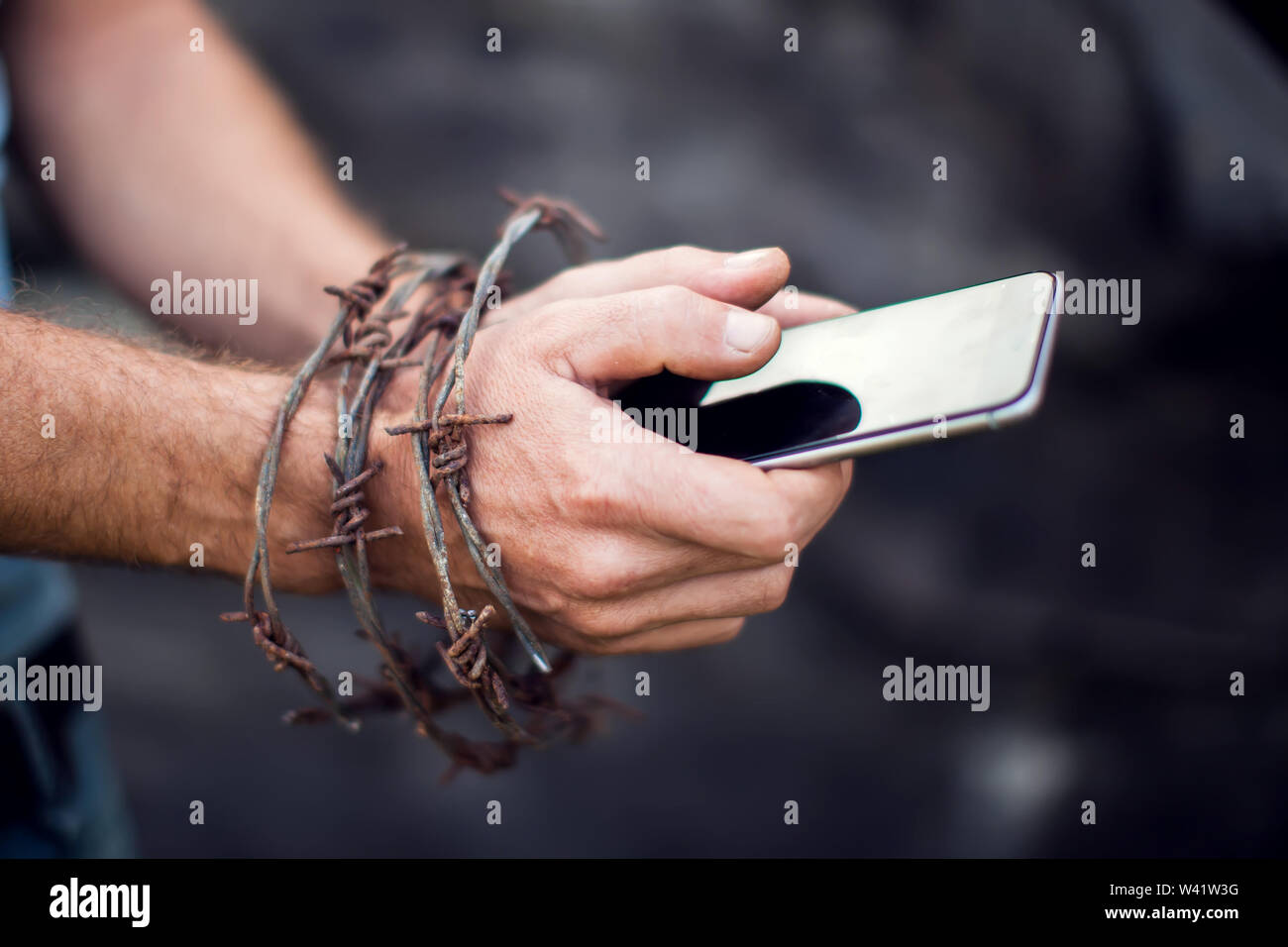 Smartphonein hands with barbed wire on a dark background. Concept of ...