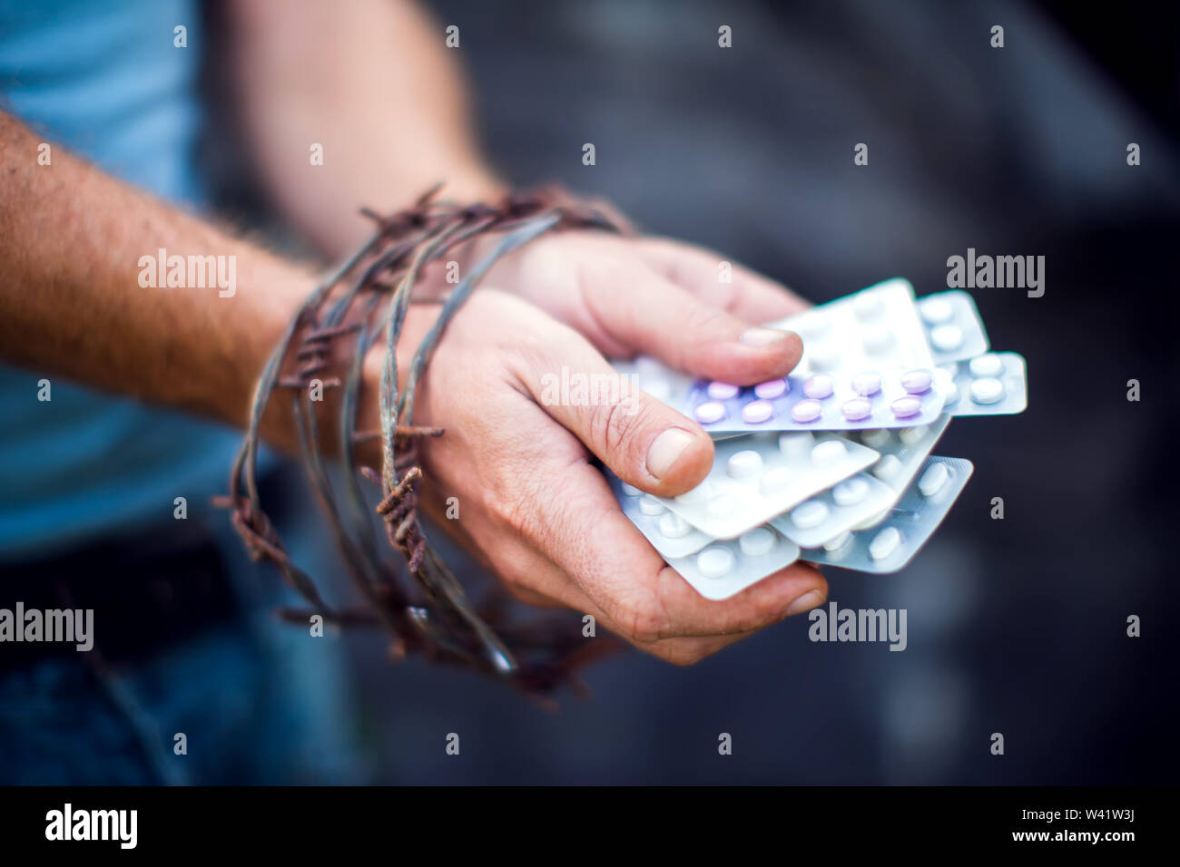 Pills in hands with barbed wire on a dark background. Concept of drugs ...