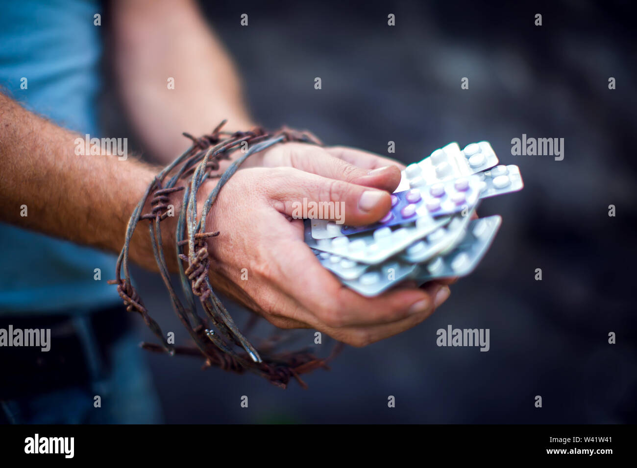 Pills in hands with barbed wire on a dark background. Concept of drugs ...