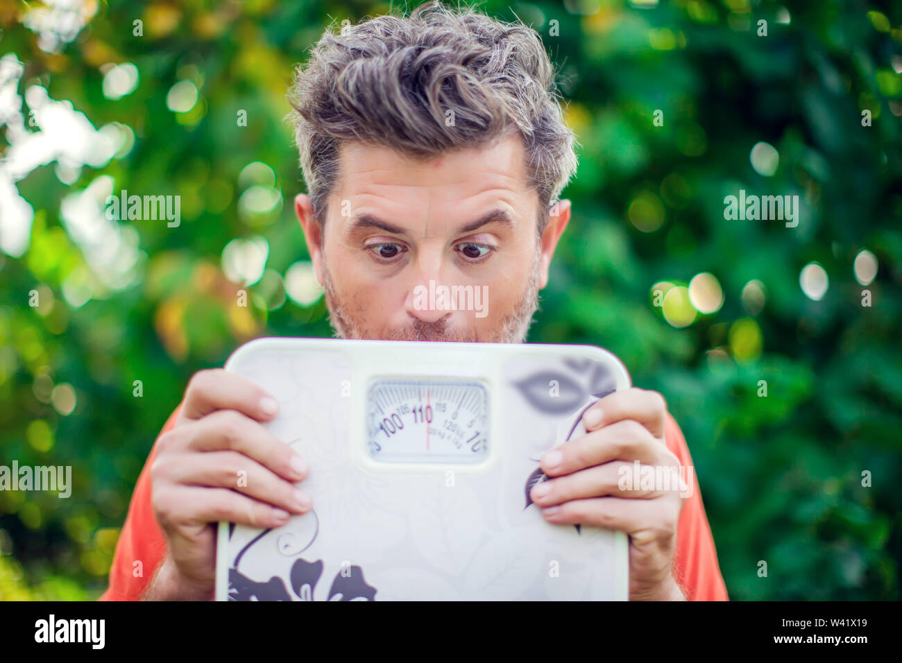 Man holding scales and looking with wondering outdoor on green ...
