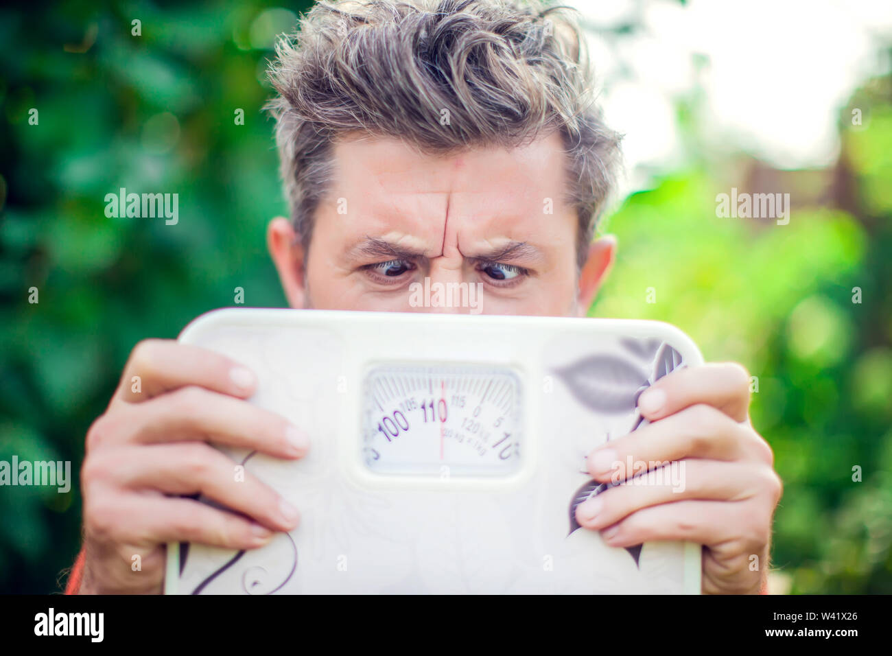 Man holding scales and looking with wondering outdoor on green ...