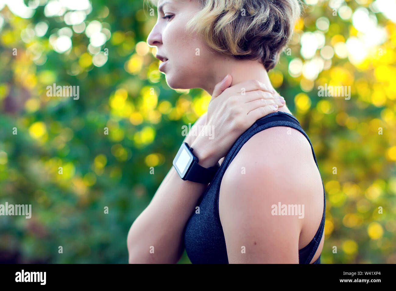 Woman in sportswear touching her neck by painful injury, over a nature ...